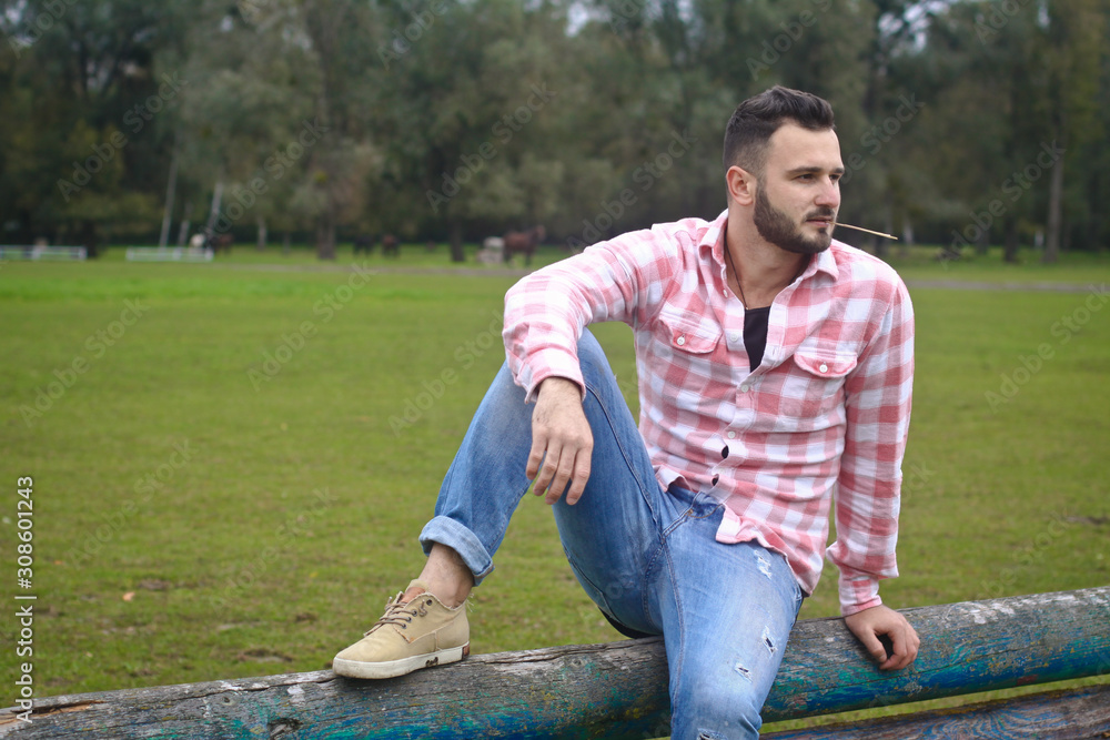 Young handsome guy Cowboy. male farmer is sitting on his fence on his ...