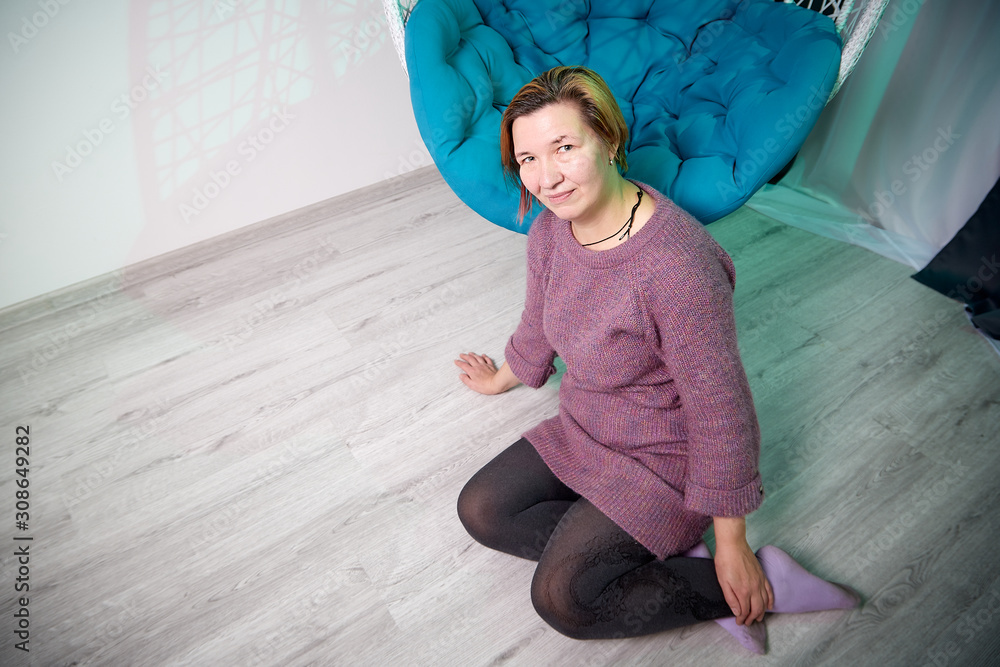 Ugly aged woman in a sweater on the floor near white wicker hanging ...