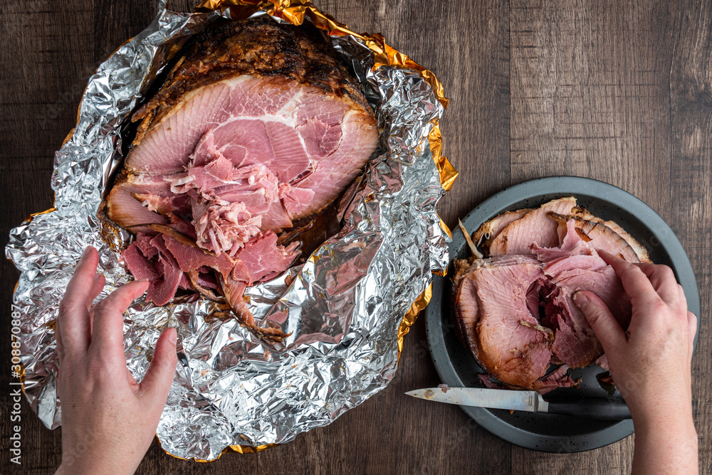 Woman’s hand pulling pieces of ham off a Spiral cut glazed and cooked ...