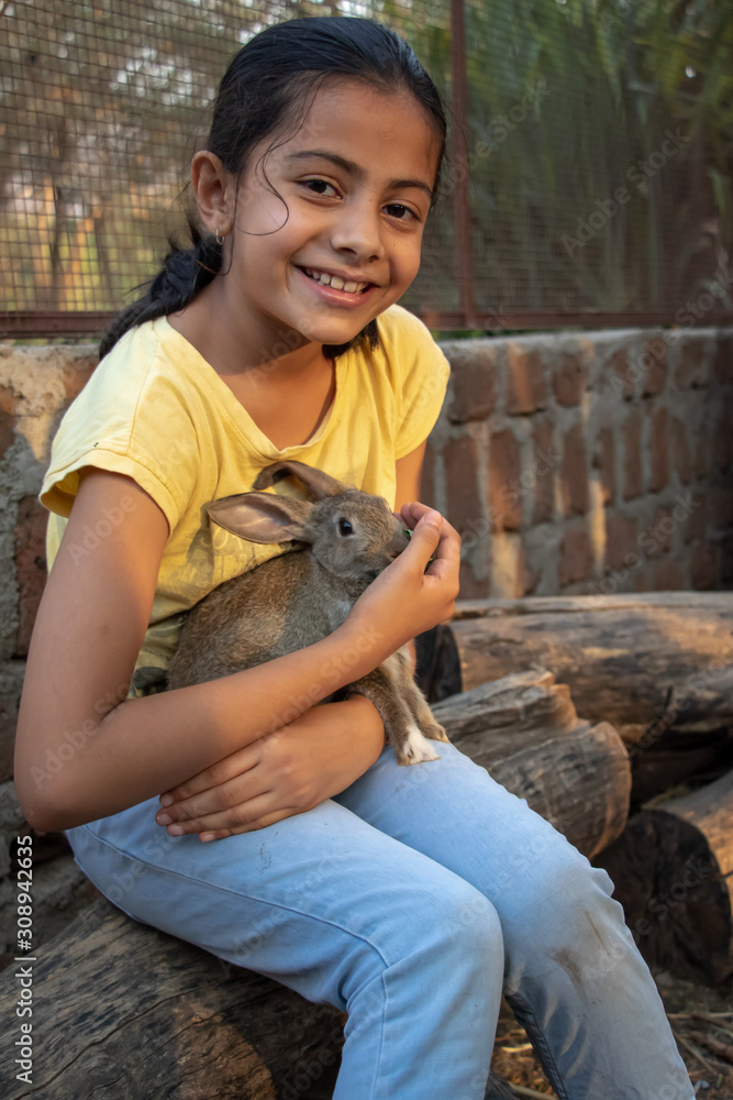 young girl sitting on bench in the park petting a rabbit and smiling ...