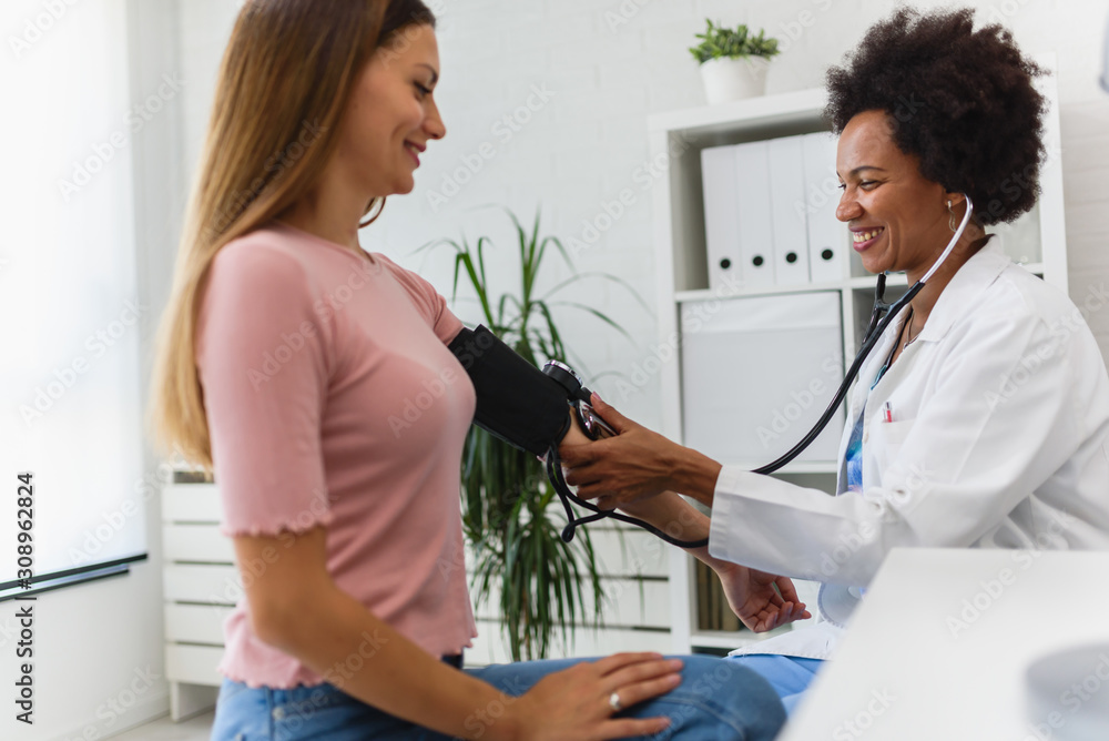 Female African American doctor measuring blood pressure of a young ...