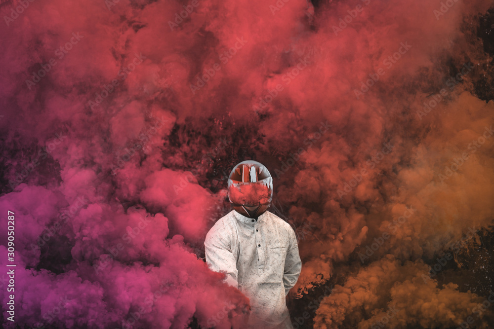 guy in mask standing in between pink, purple and orange smoke bombs ...