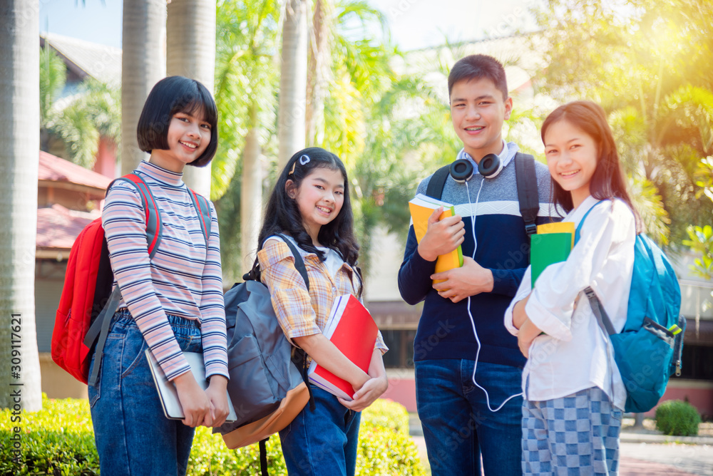 Four asian teenager students standing in park and smiling at camera ...