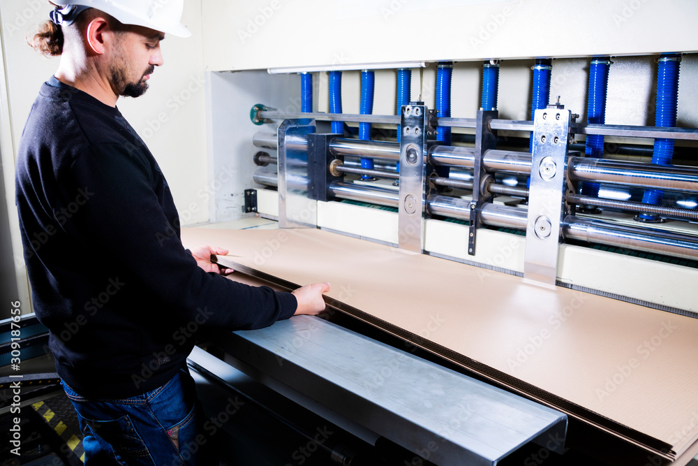 Cardboard boxes production. Worker in a hard hat holding cartons in his ...