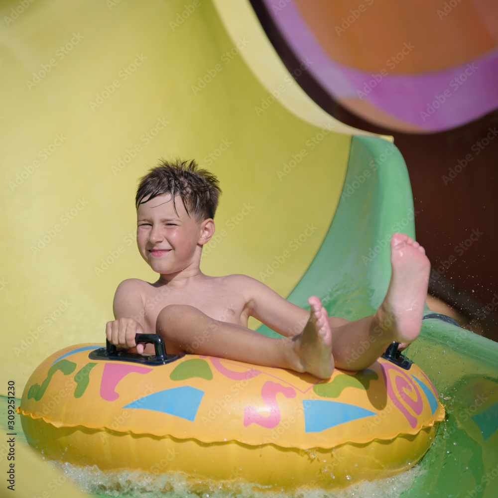 Boy on floater sliding down slide in waterpark. He is enjoying his ...