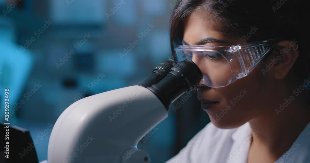 Female research scientist looking into microscope, wearing safety ...