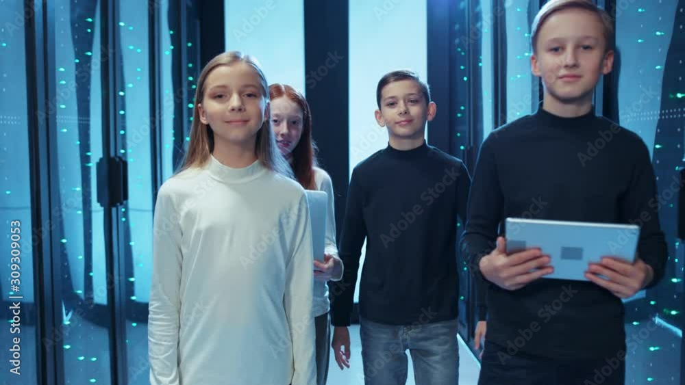 Smart adorable teenagers standing in row at operational server cabinet ...