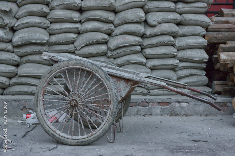 Old construction barrow standing in front of cement and sand bags pile ...