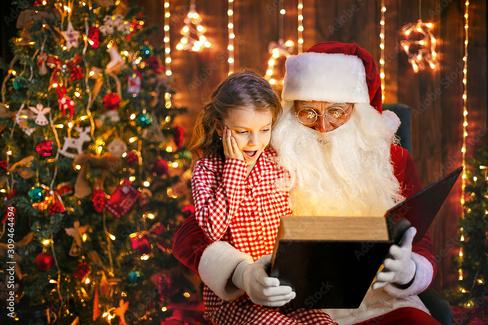 Santa Claus open and read magic book with little cute amazed girl in ...