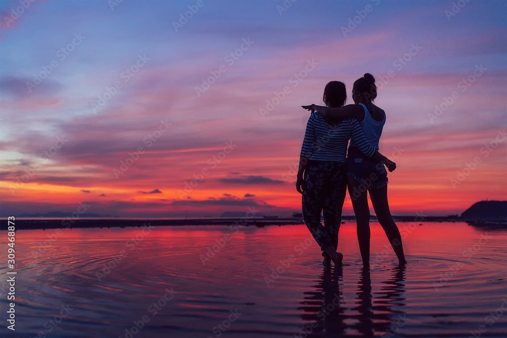 Two girlfriends hugging up and enjoying a rose/pink sunset sky on the ...