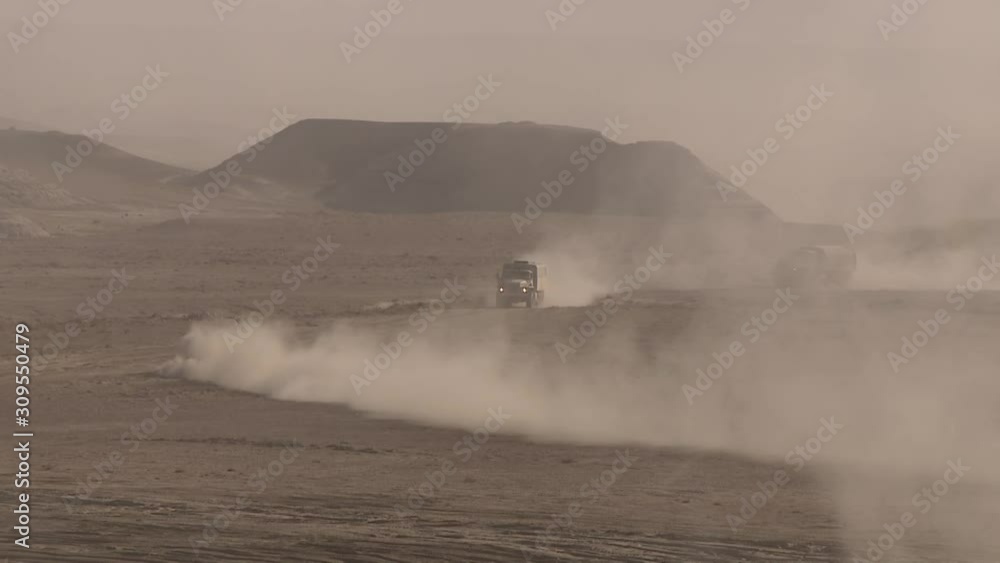 Military cargo convoy rides fast in desert sand dunes, leaving behind a ...