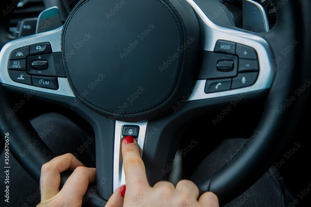 the finger of a female hand points to the heated steering wheel button ...