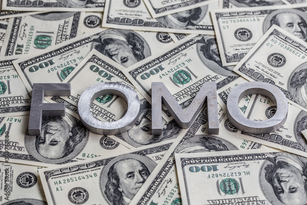 The word FOMO laid with aluminium letters on the US dollar banknotes ...