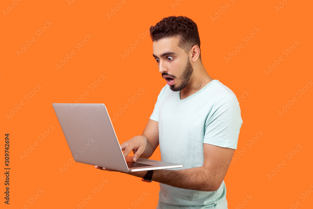 Portrait of young bearded man shocked by message on laptop, having ...