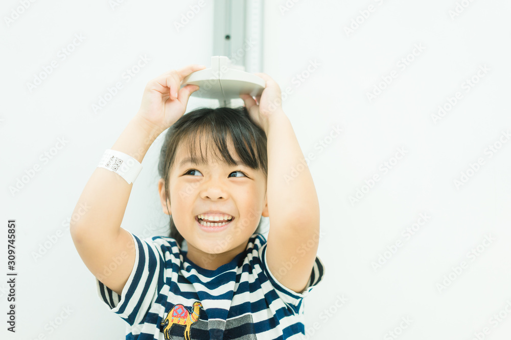 Little asian girl measuring her height near white wall in hospital.5 ...