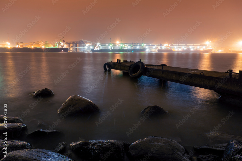 Night seaport. Pier on the smooth surface of the water. Stones on the ...