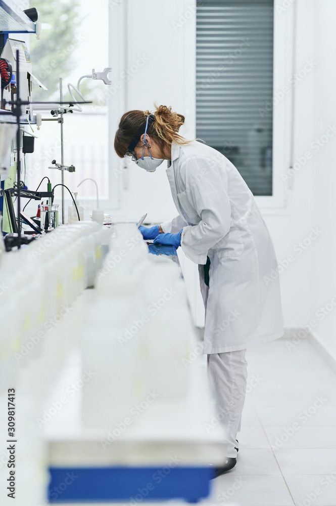 A female scientist wearing a safety mask, white robe and blue lab ...