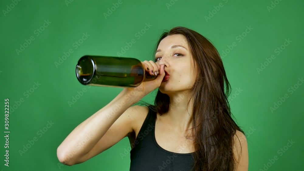 Cute drunk girl with long hair is drinking wine from dark bottle on ...