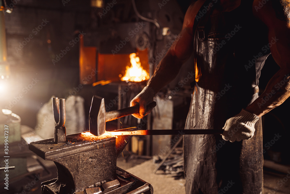 Photo & Art Print young bearded man in leather uniform heats the metal ...