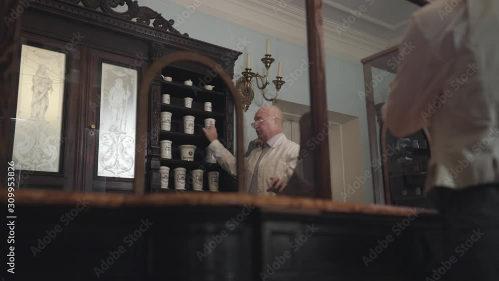 Old wise Caucasian pharmacist in eyeglasses showing at old-fashioned ...