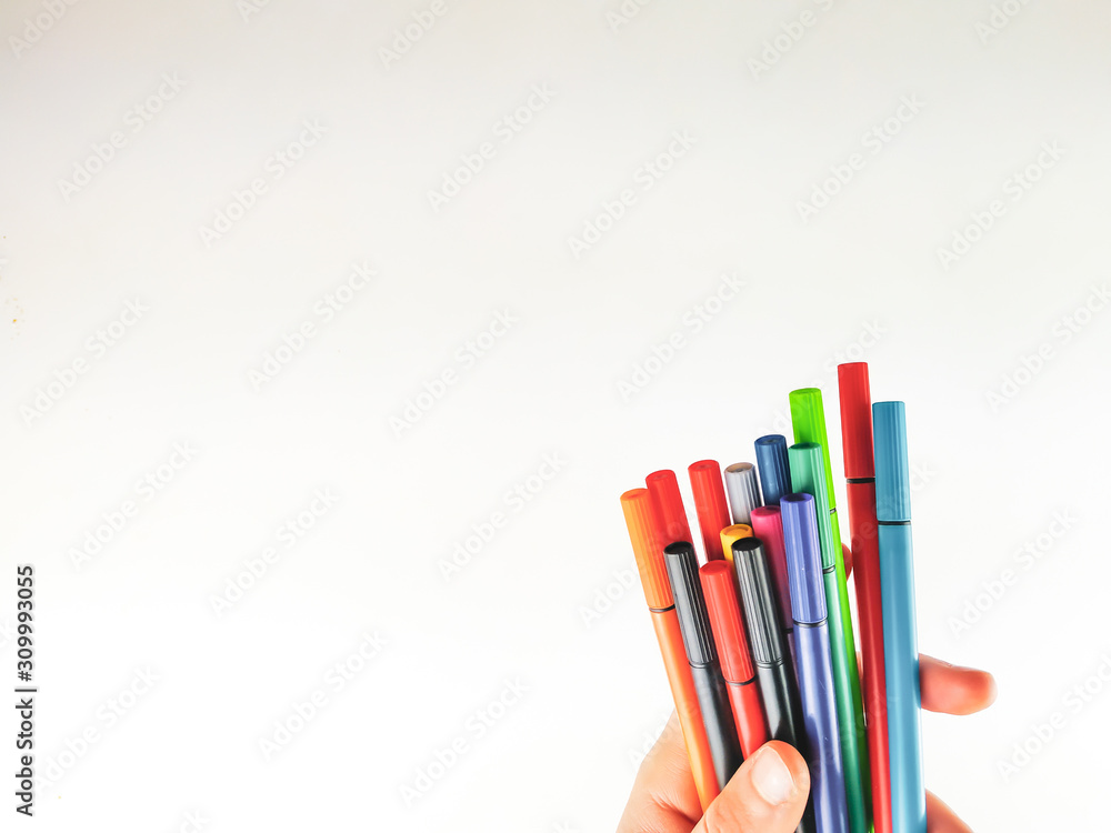 Closeup and side view of a hand holding many pens in different colors ...