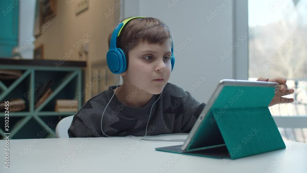 School boy with autism playing on tablet computer in color headphones ...