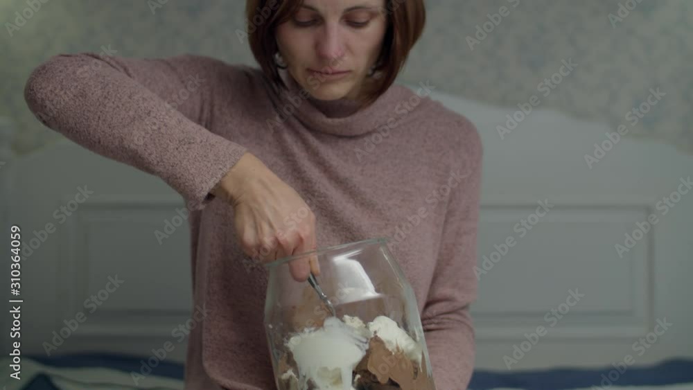 Crying young brunette woman eating vanilla and chocolate ice cream ...