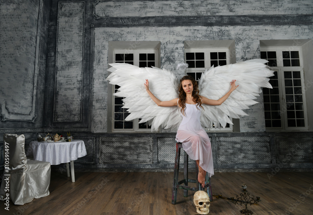 white angel in a thoughtful pose sits on a chair spreading its wings ...