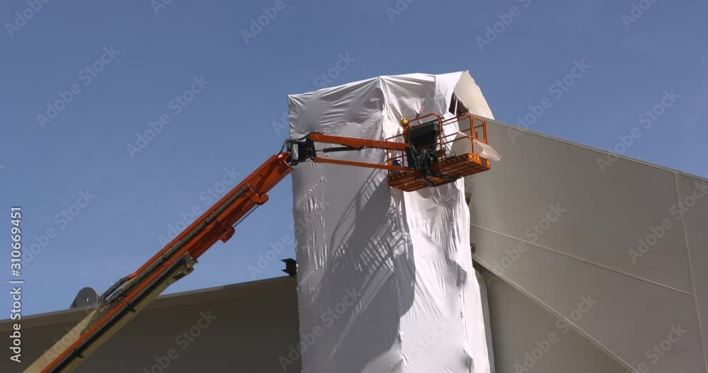 Scaffolder on an elevated work platform shrinks wrap to a scaffolding ...