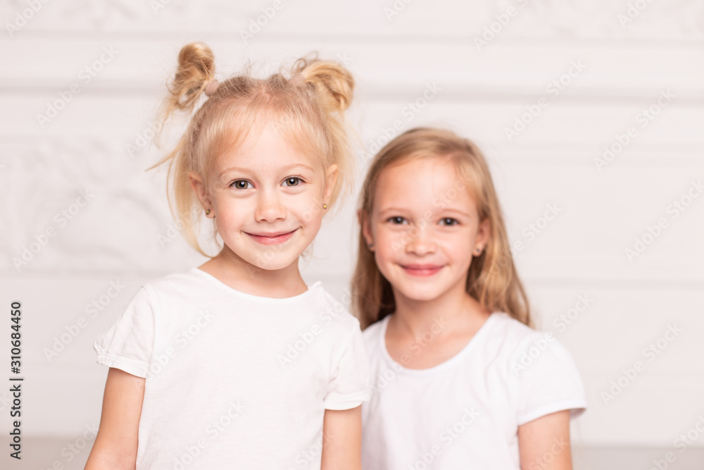 Two little cute sisters pose for a photo standin next to each other ...