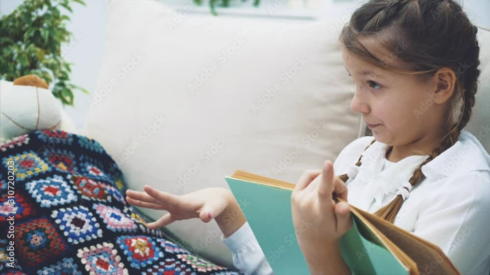 Cute little girl sitting with her legs curled up, reading fairy-tale ...