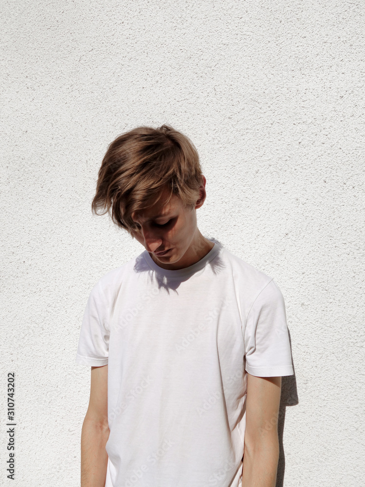 Portrait of a young guy of model appearance standing near a white wall ...