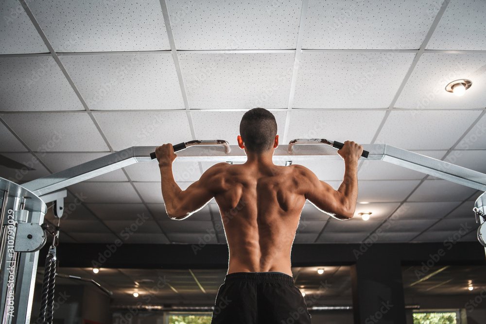 A young athlete trains his back muscles on a horizontal bar with a wide ...