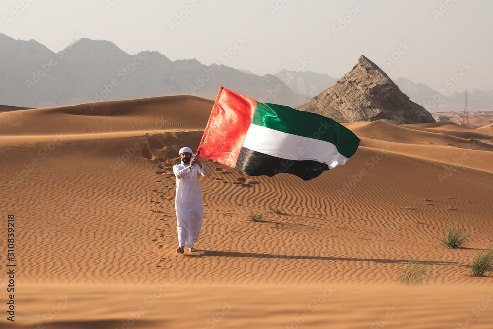 Arab man holding the UAE flag in the desert celebrating UAE national ...