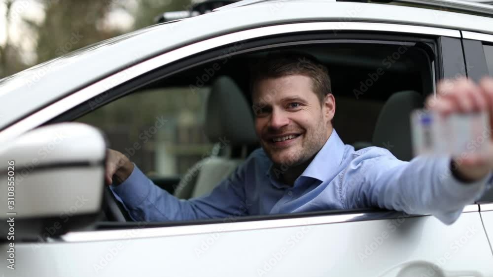young man sitting in the car and showing his new driver license with ...