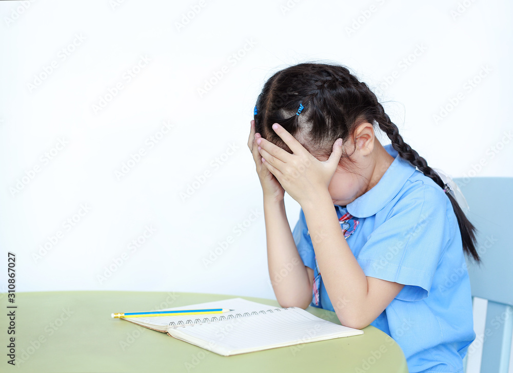 Stressed little girl in school uniform sitting at desk isolated over ...