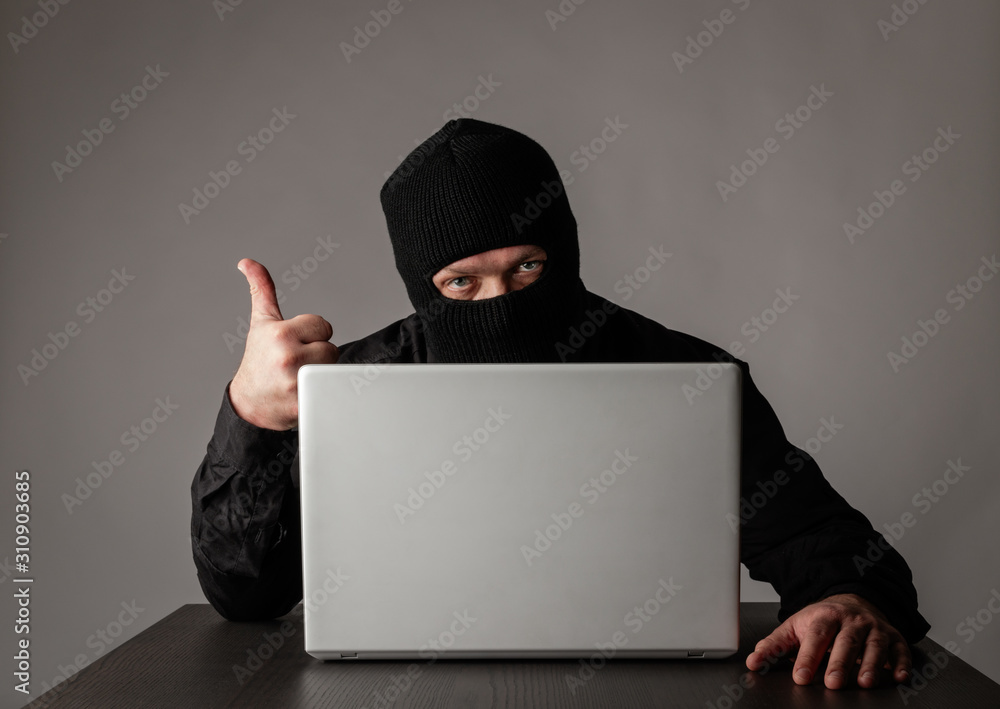 Hacker in mask using a laptop. Stock Photo | Adobe Stock