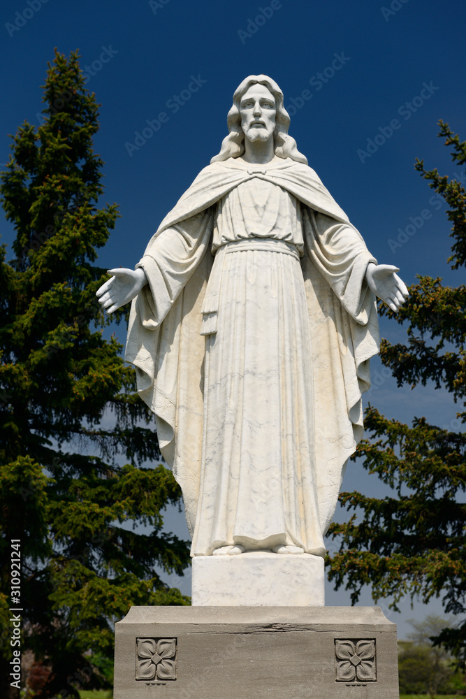 Marble statue of Jesus Christ the Saviour outdoors with spruce trees ...