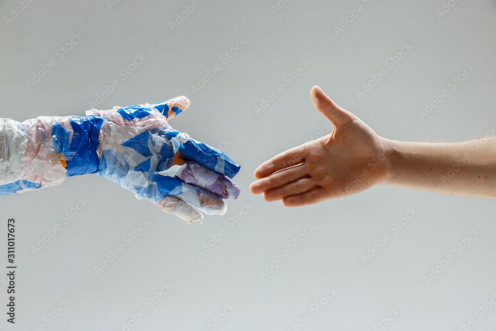 Big plastic hand made of garbage shaking another hand on white studio ...