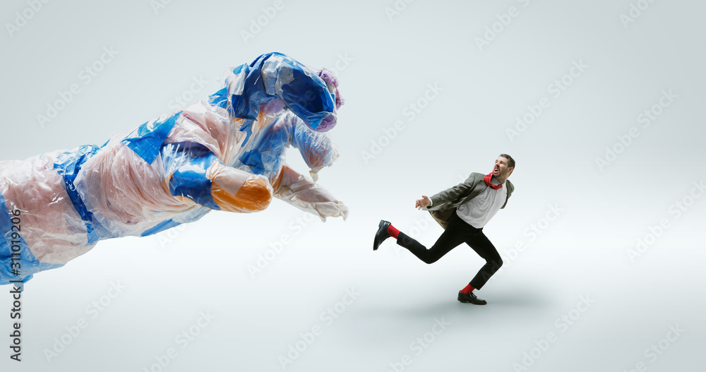 Young caucasian man avoiding big plastic hand on white studio ...