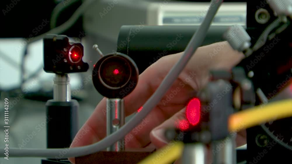 laser setup in photonic lab. laser beam. hand is placing lens to direct ...