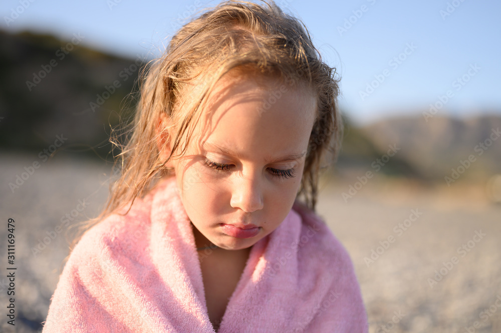 sad six year old little girl resting on the sea beach after swimming ...