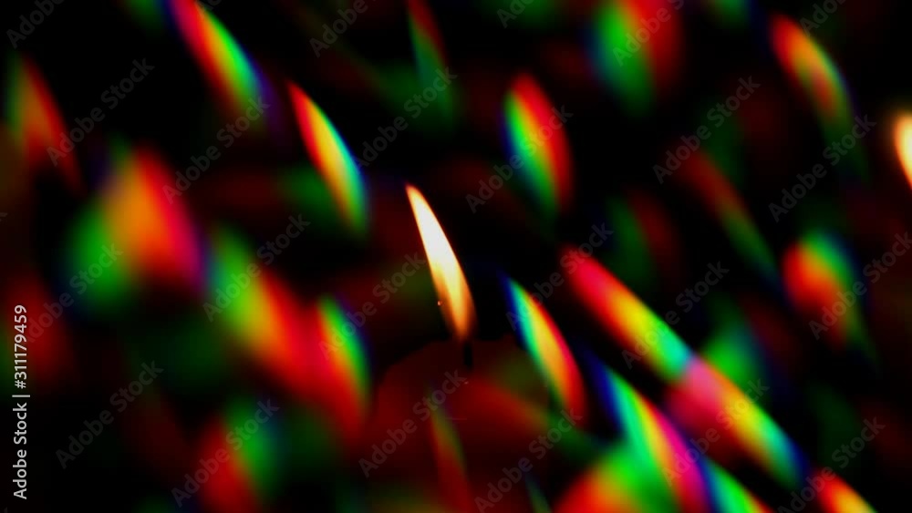 Flame of a candle surrounded by a halo of multi-colored glares, was ...