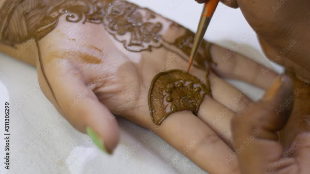 Closeup shot of a mehndi (heena) artist applying mehndi on the hands of ...
