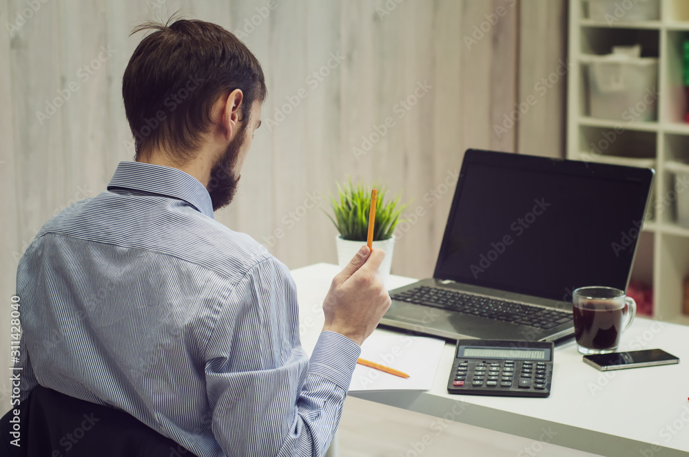 Thinking man sits by the table and working, holds in hand a pencil ...
