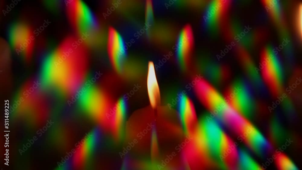 Flame of a candle surrounded by a halo of multi-colored glares, was ...