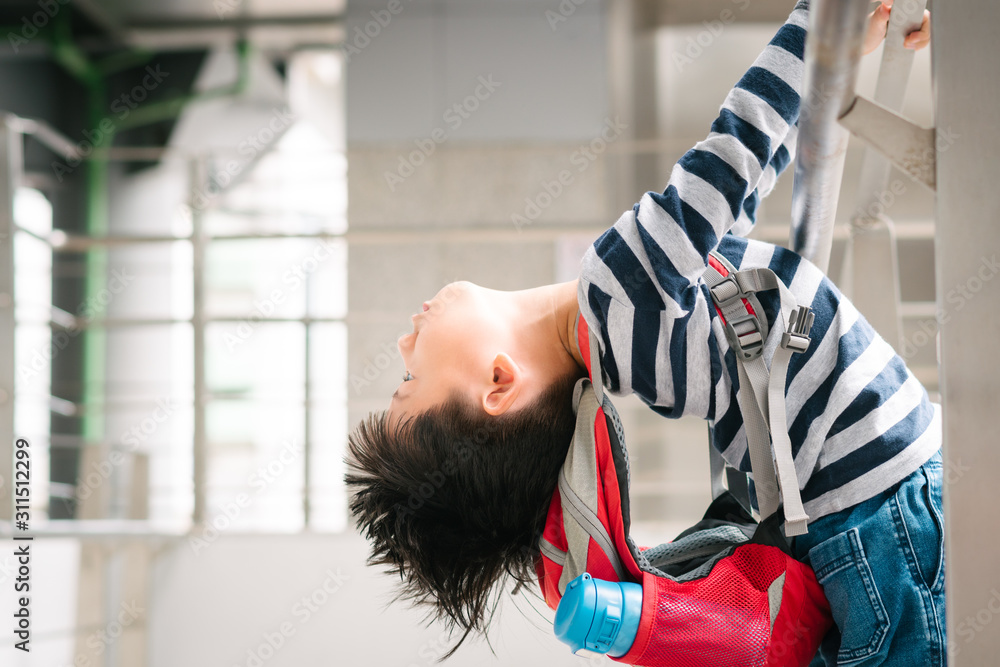 Little Asian hyperactive difficult boy hold handrail and lean body and ...
