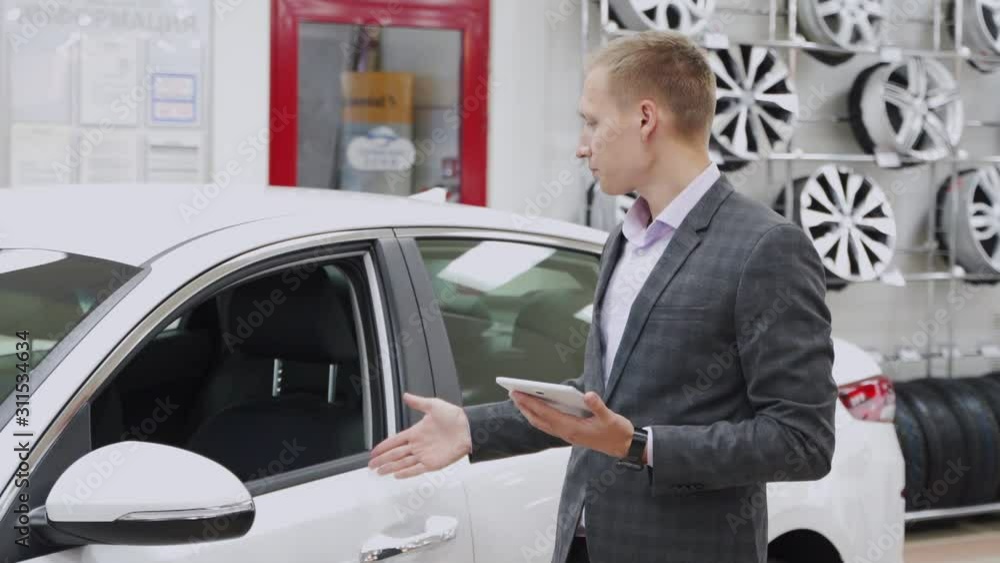 Man seller with tablet shows the car in the showroom. Successful ...