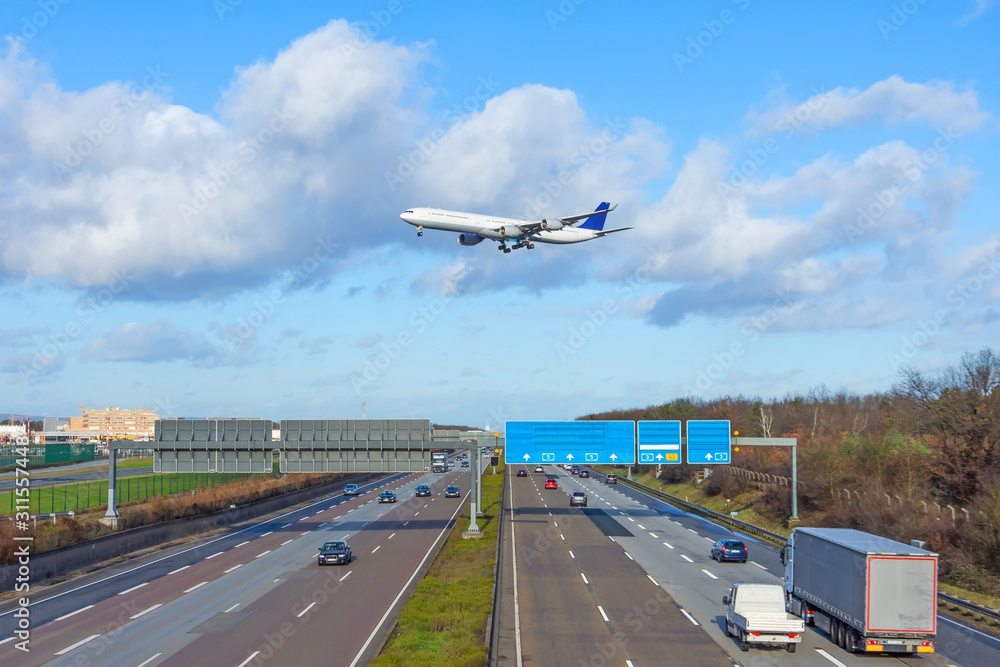 Landing airplane flies over a high-speed highway with cars in the city ...