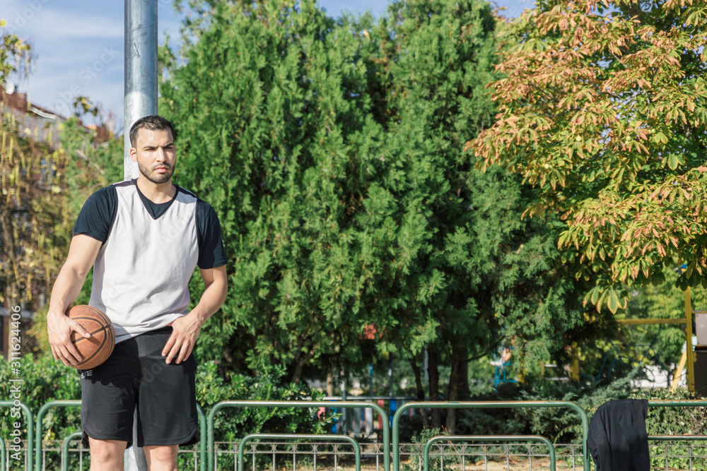 Attractive urban basketball player leaning on a metal column on a court ...